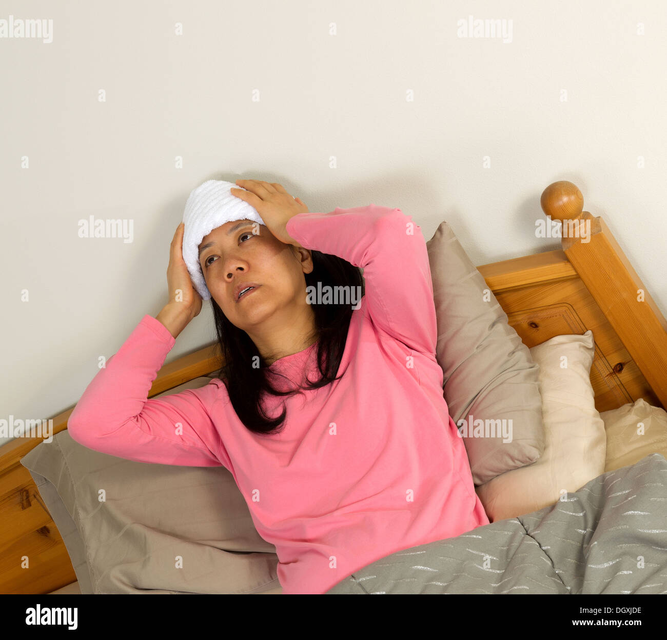 Photo of mature woman treating fever by holding wash cloth to her ...
