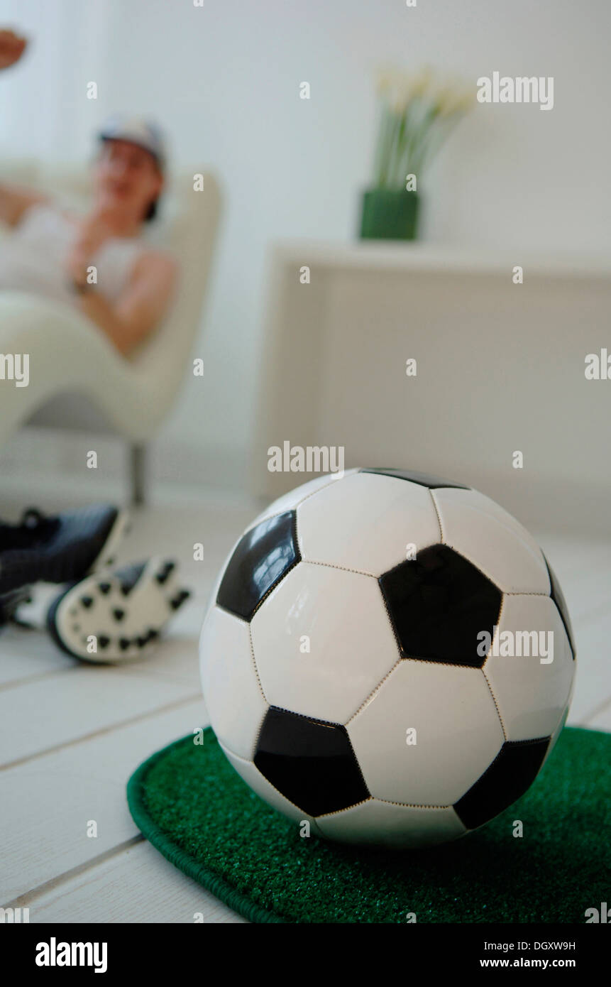 Football lying on grass carpet in the living room, football fan sitting ...