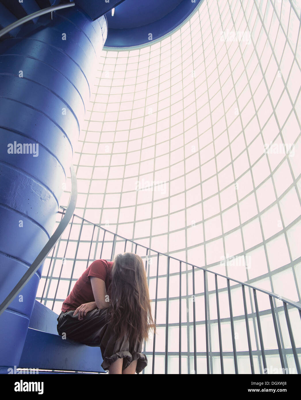 Woman with long hair sitting on the stairs of a staircase with glass ...