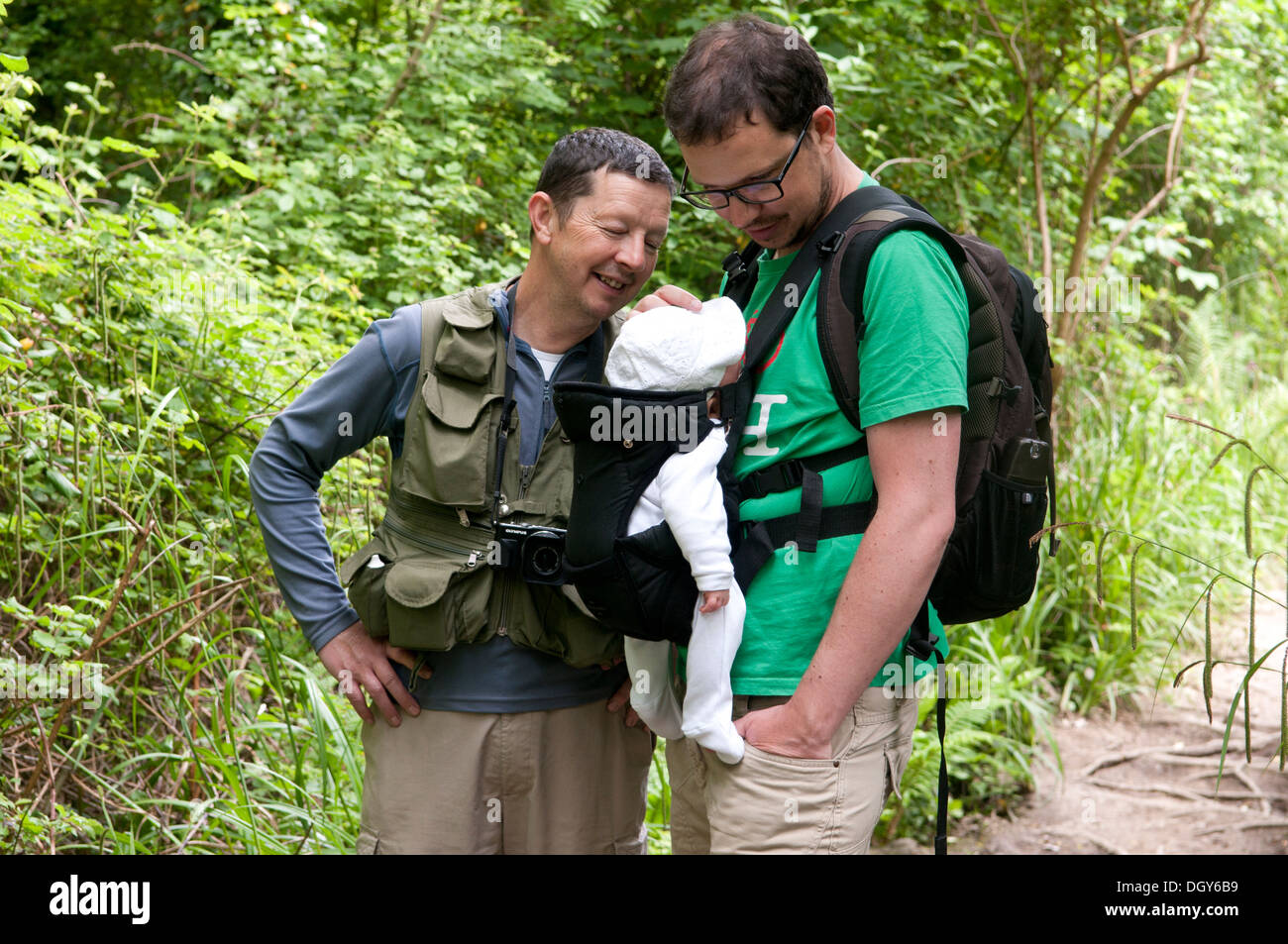 Father and son carrying his little baby in a sling enjoying a walk in ...