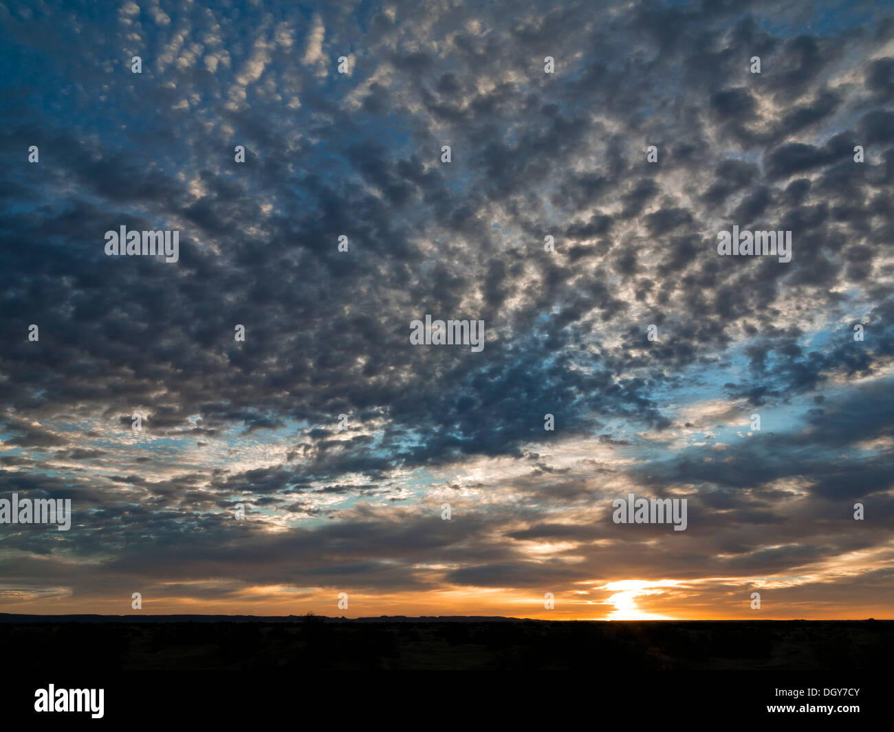 Sunrise over a desert horizon with mottled sky and diffused sun disc ...