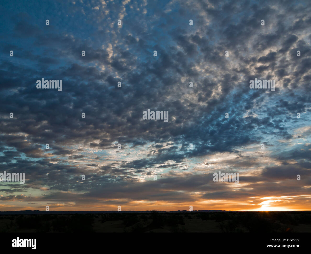 Sunrise over a desert horizon with mottled sky and diffused sun disc ...