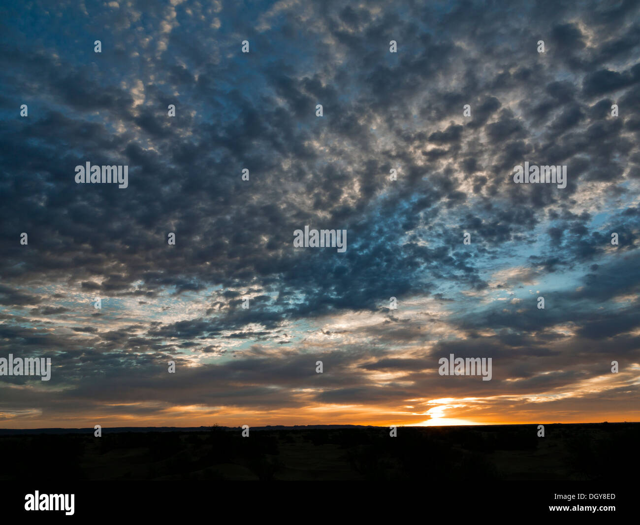 Sunrise over a desert horizon with mottled sky and diffused sun disc ...