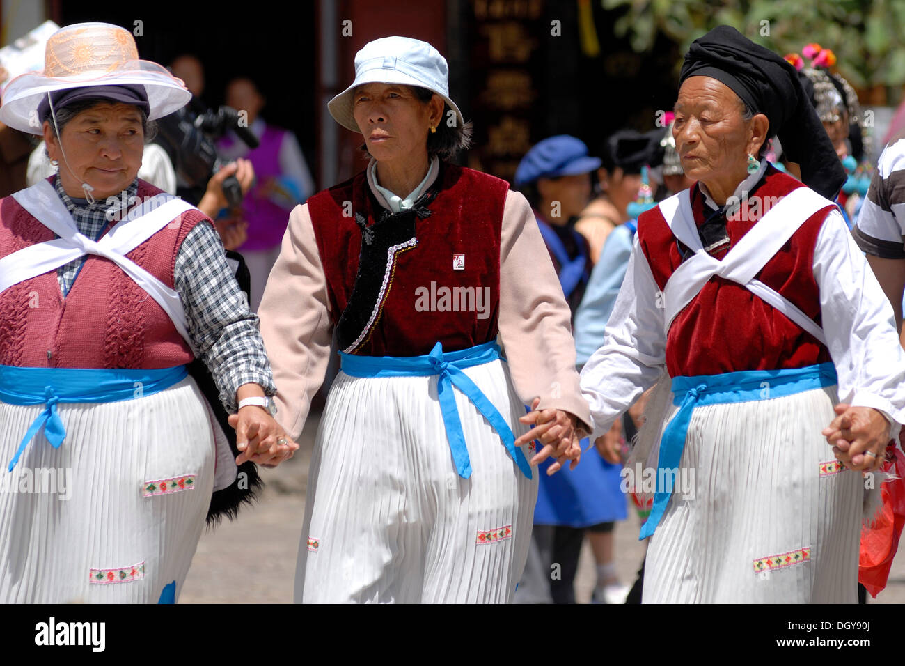 Three women in traditional costume of the Naxi minority holding hands ...