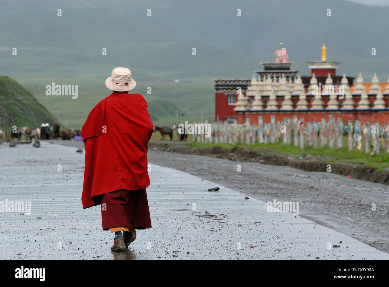 Tibetan monk in a red robe walking in the rain on a road to a Tibetan ...