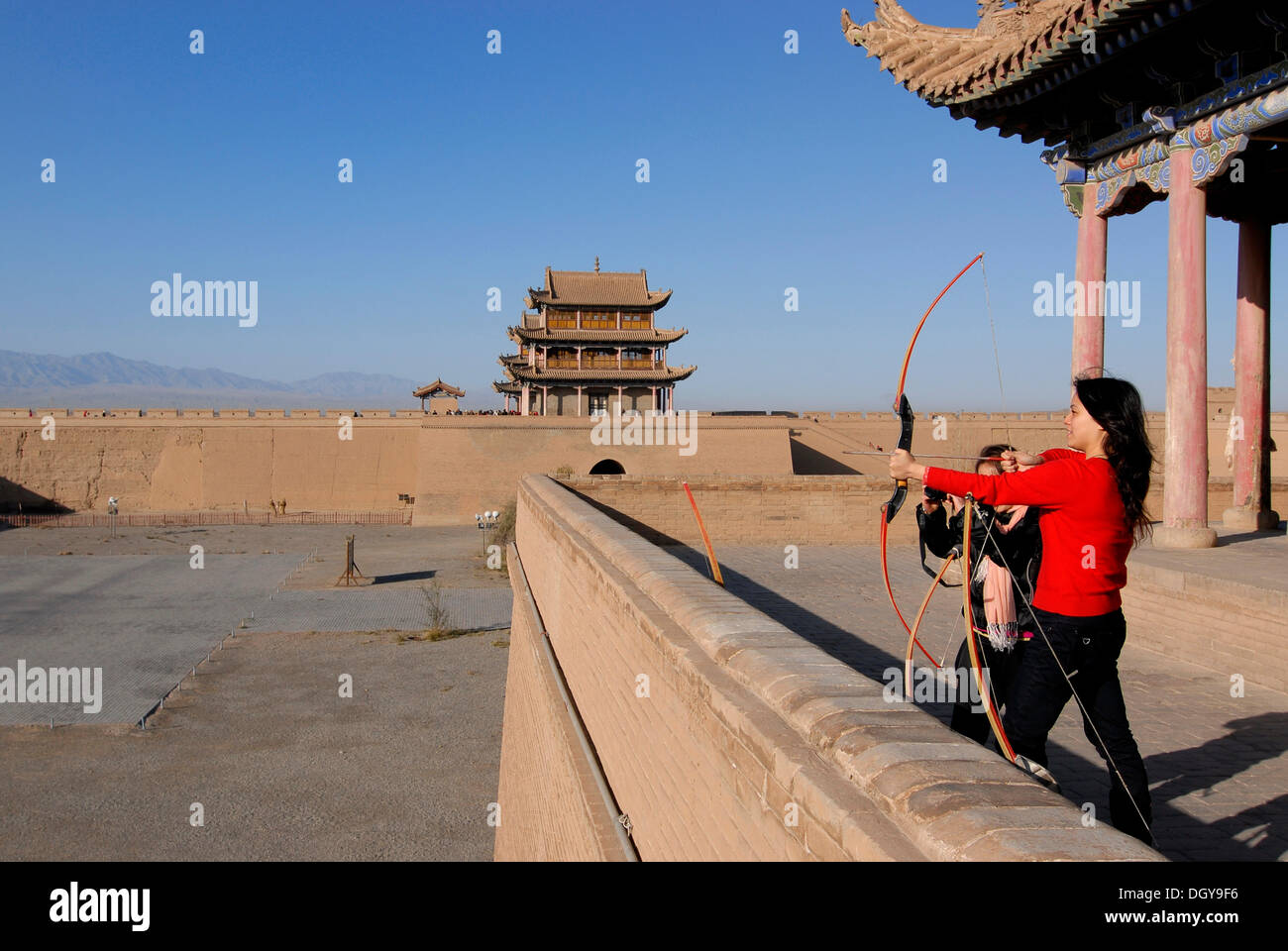 Chinese woman using a bow and arrow at the Jiayuguan Fortress with two ...