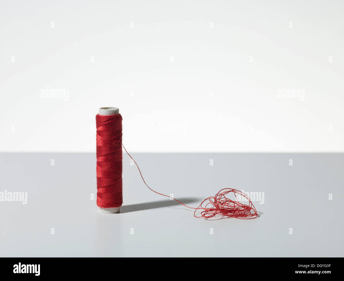 A spool of red thread with a pile of tangled thread Stock Photo - Alamy