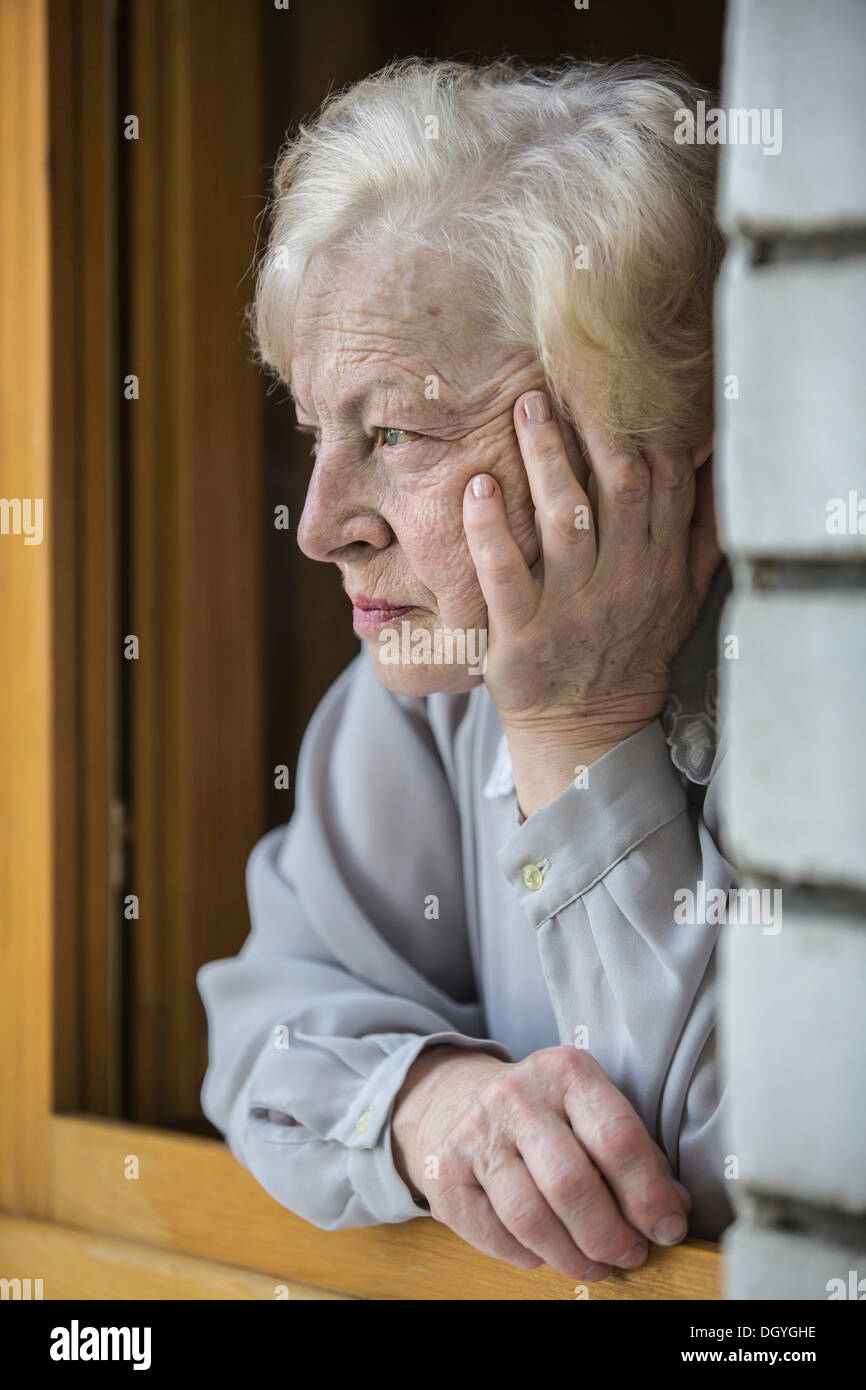 A senior woman leaning on a window sill, looking contemplative Stock ...