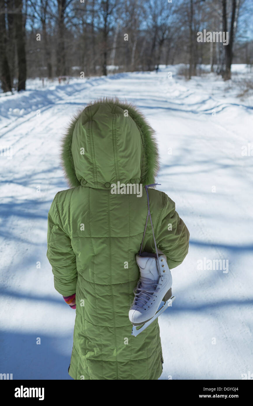 A young girl standing on a snowy road with an ice skate slung over her ...