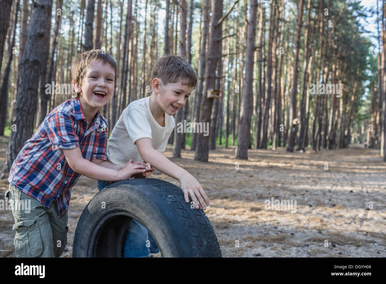 Two young boys pushing a tire in a wooded area Stock Photo - Alamy