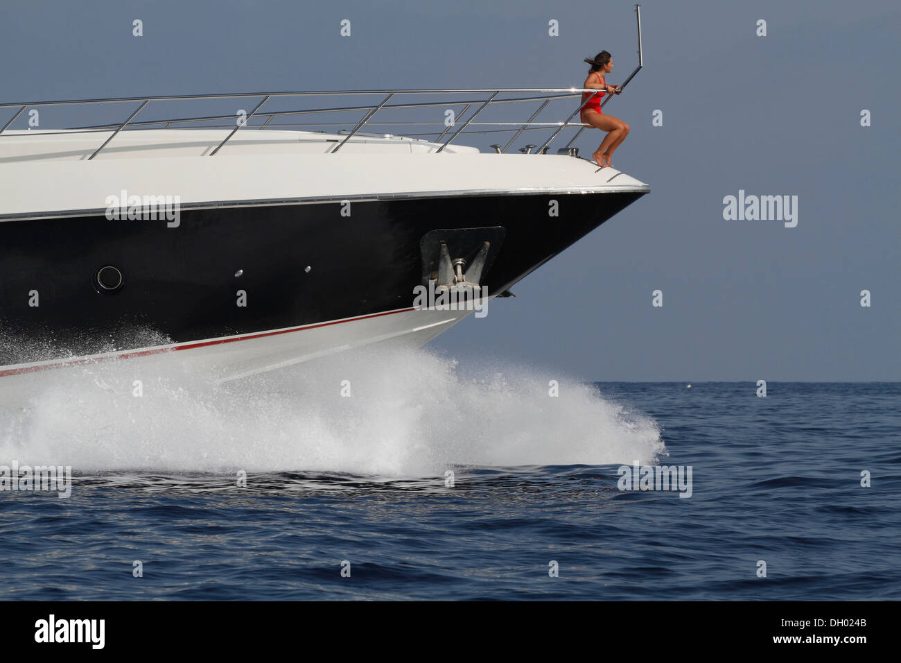 Young woman wearing a red swimsuit sitting on the railing of the bow of ...