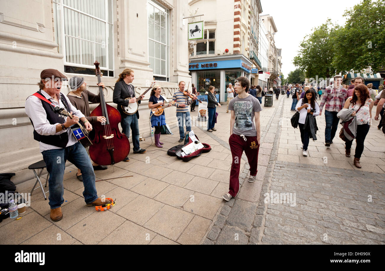 People walking past a folk band busking on the street, Norwich, Norfolk ...