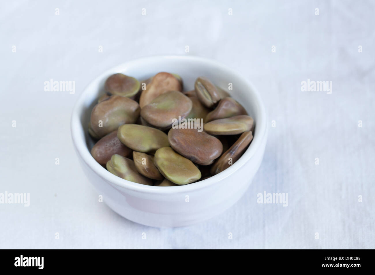 Dried fava beans in white bowl on white cloth Stock Photo - Alamy