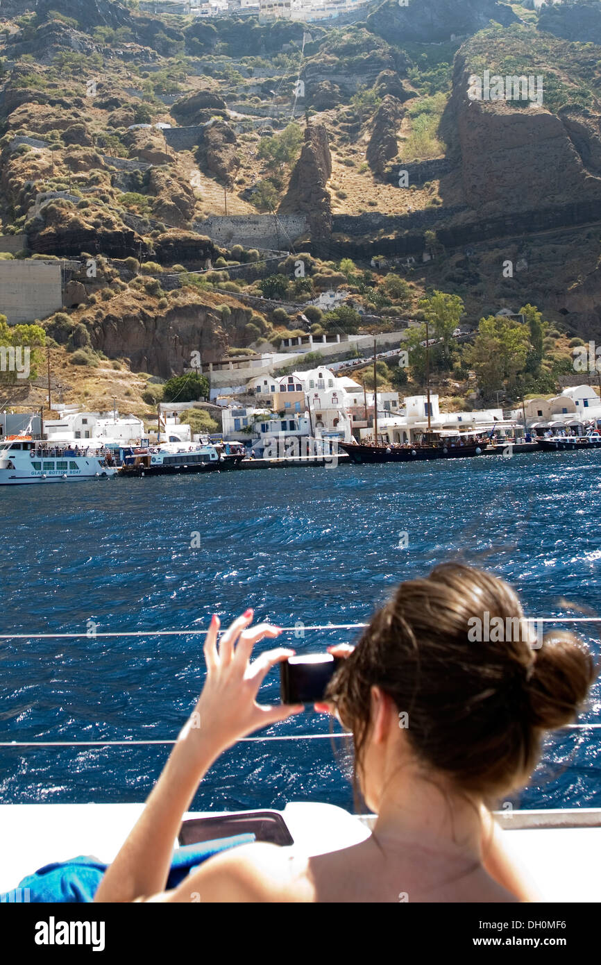 A women takes a picture of Skala Pier, the old Port of Santorini, while ...