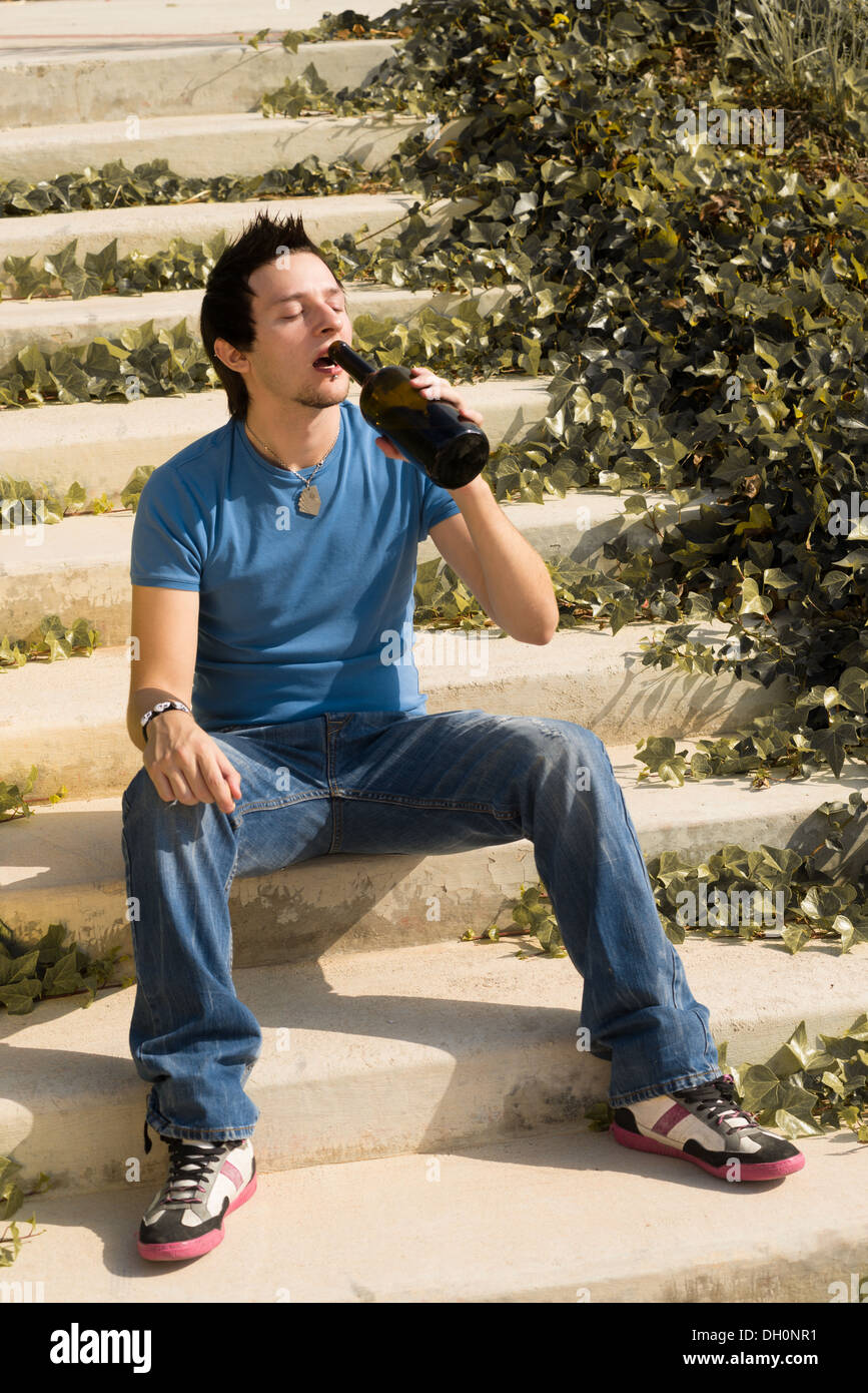 Alcohol addict drinking while sitting on some stairs in a park Stock ...