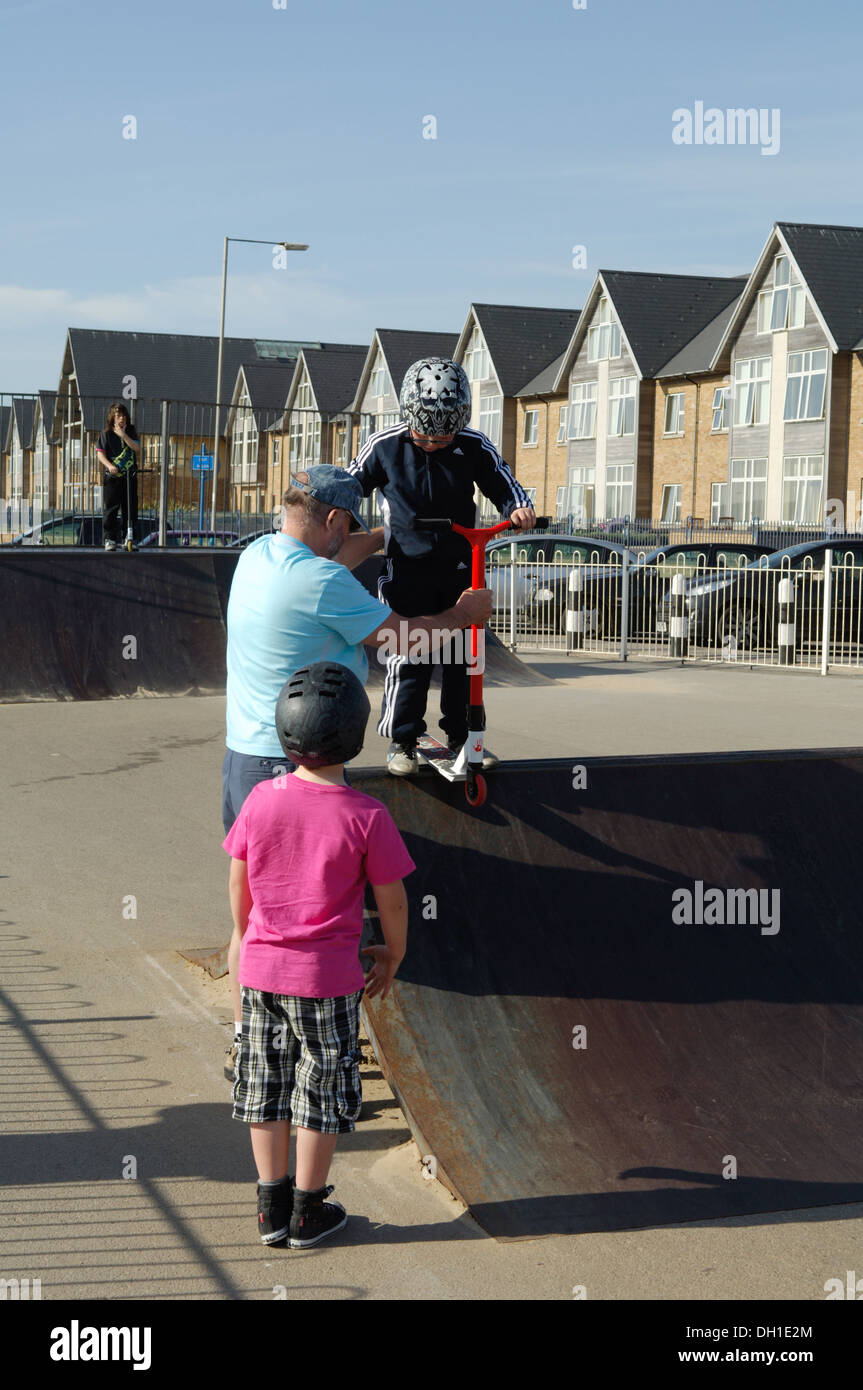 Father helping a young child on a scooter in a small skate park while ...
