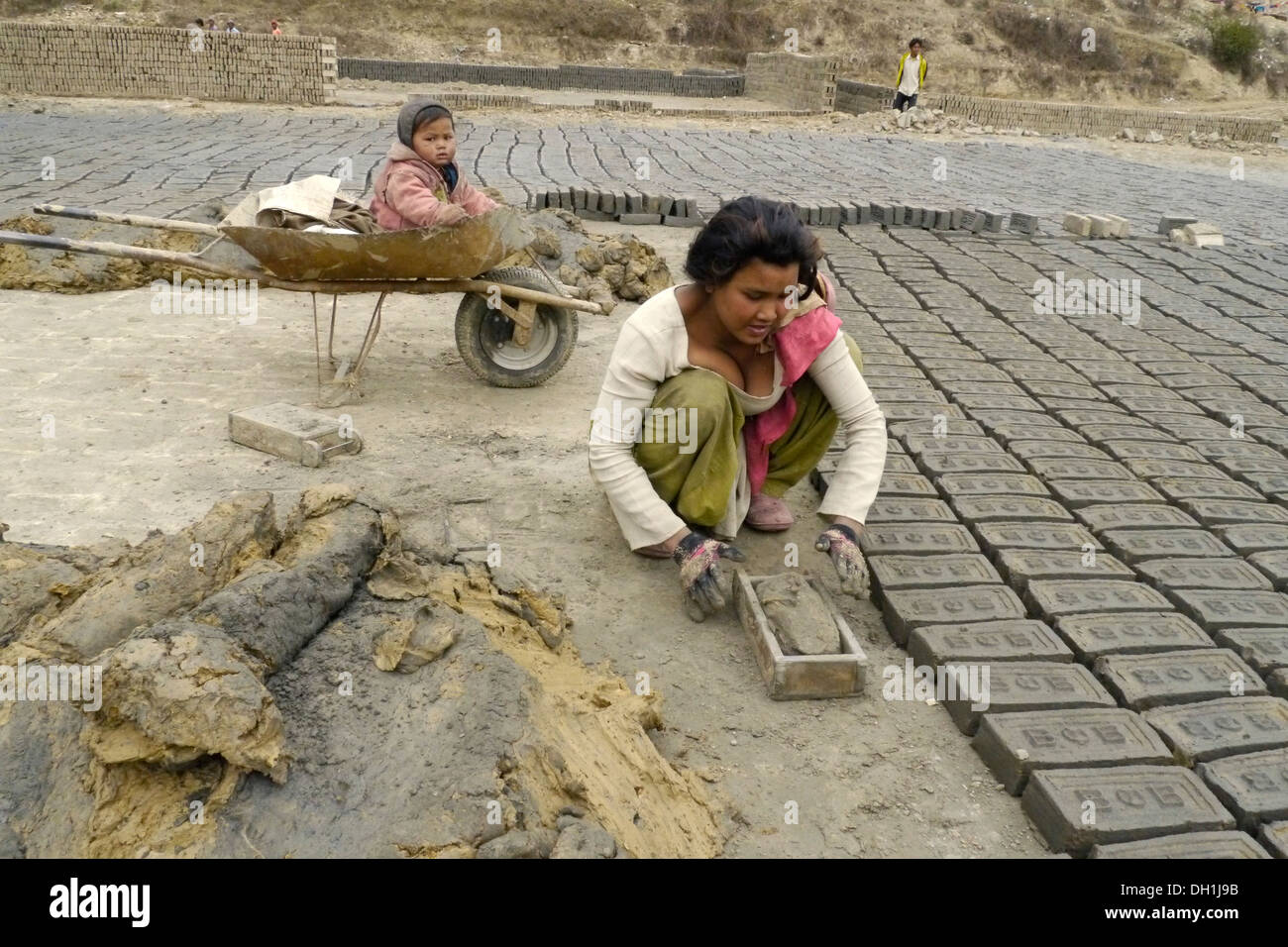 Brickmaker at work while her baby looks on from a wheelbarrow, Godavari ...