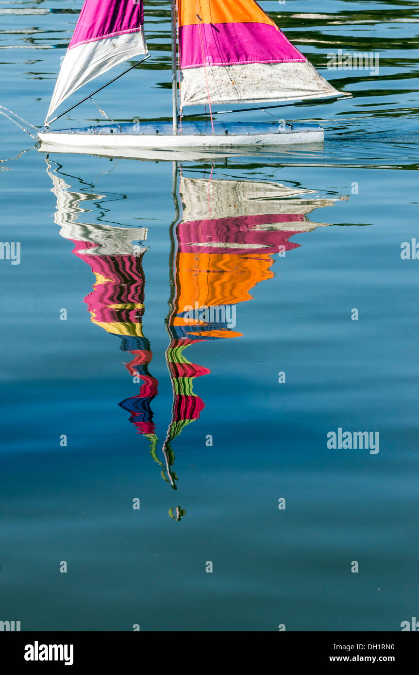 Reflections of a toy scale model sloop sailboat with colorful striped ...