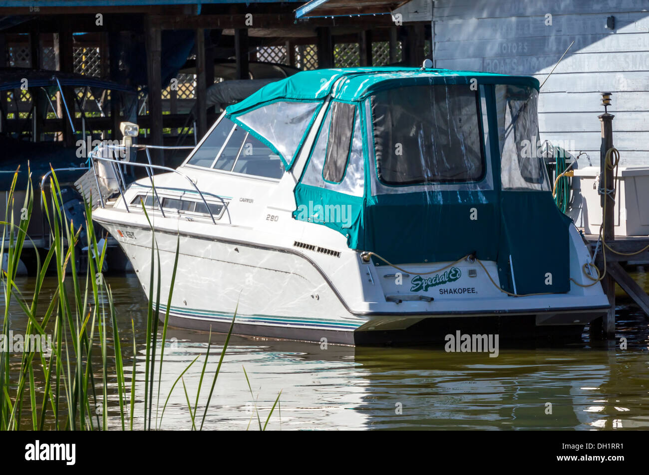 Boats and motor cruiser with turquoise canopy moored by boathouses ...