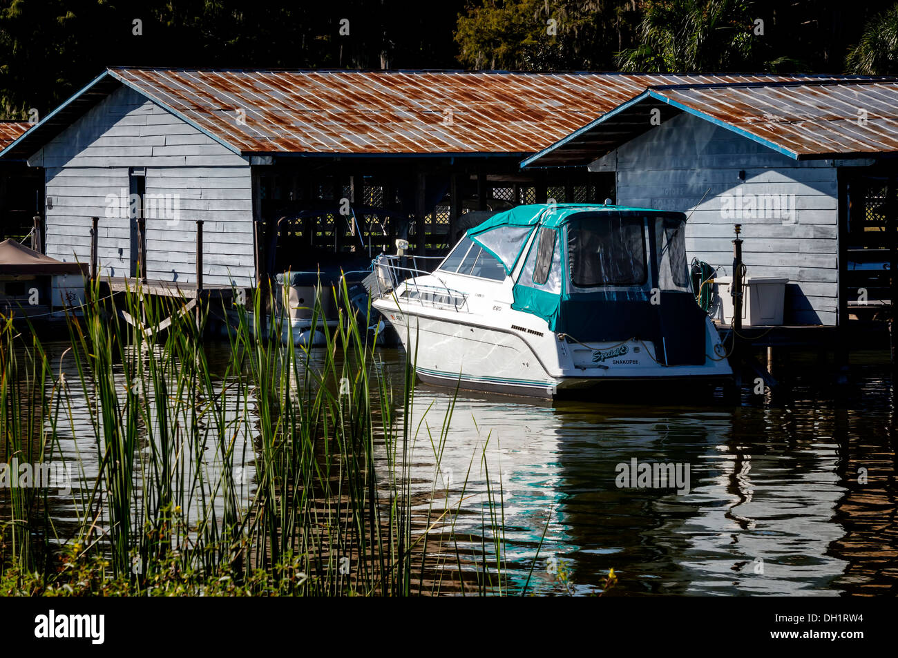 Boats and motor cruiser with turquoise canopy moored by boathouses ...