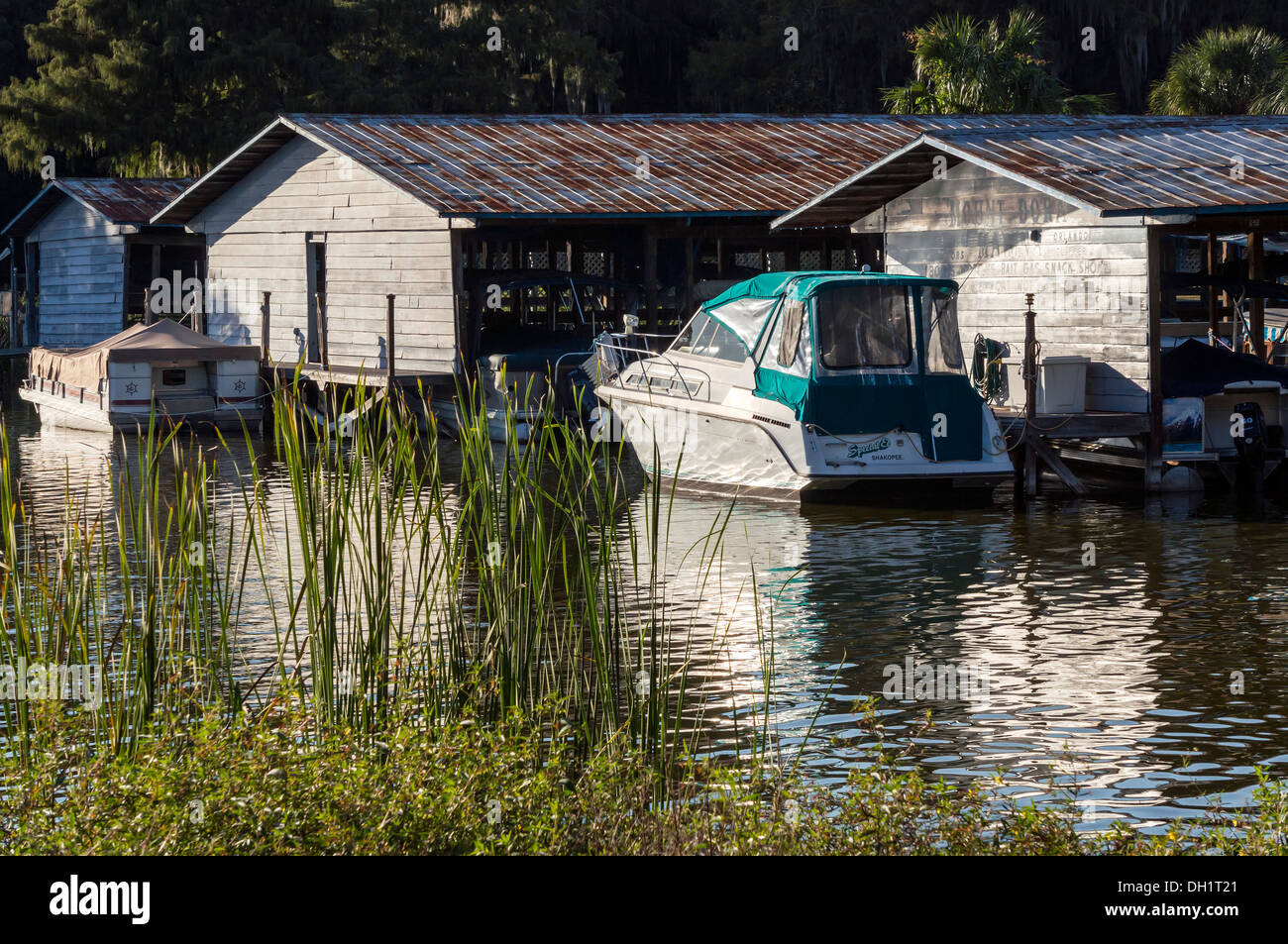 Boats and motor cruiser with turquoise canopy moored by boathouses ...