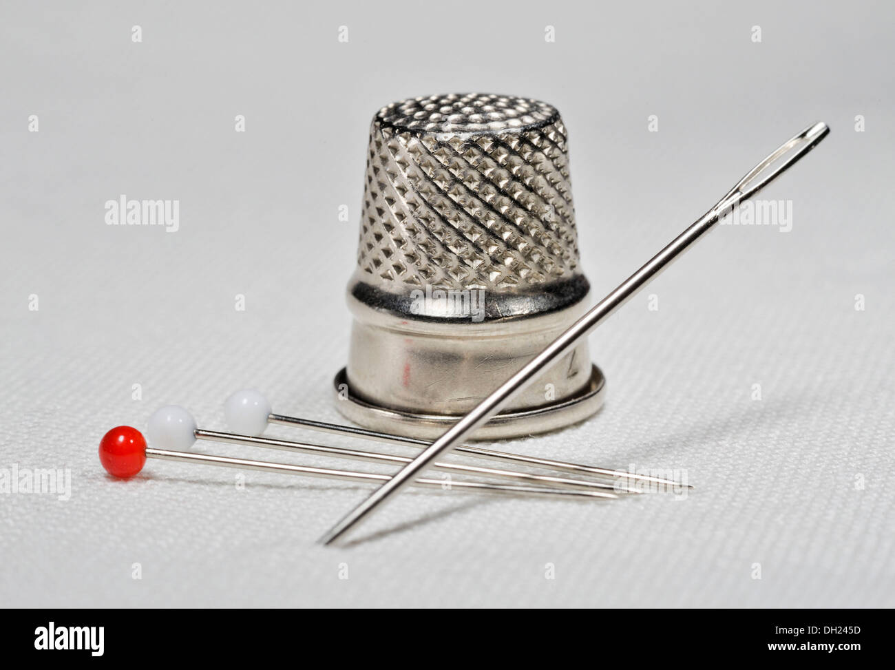 Sewing needle, pins and thimble lying on white linen fabric Stock Photo ...