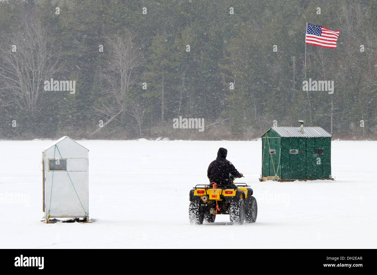 A man drives an ATV between ice fishing huts on a frozen lake during a ...