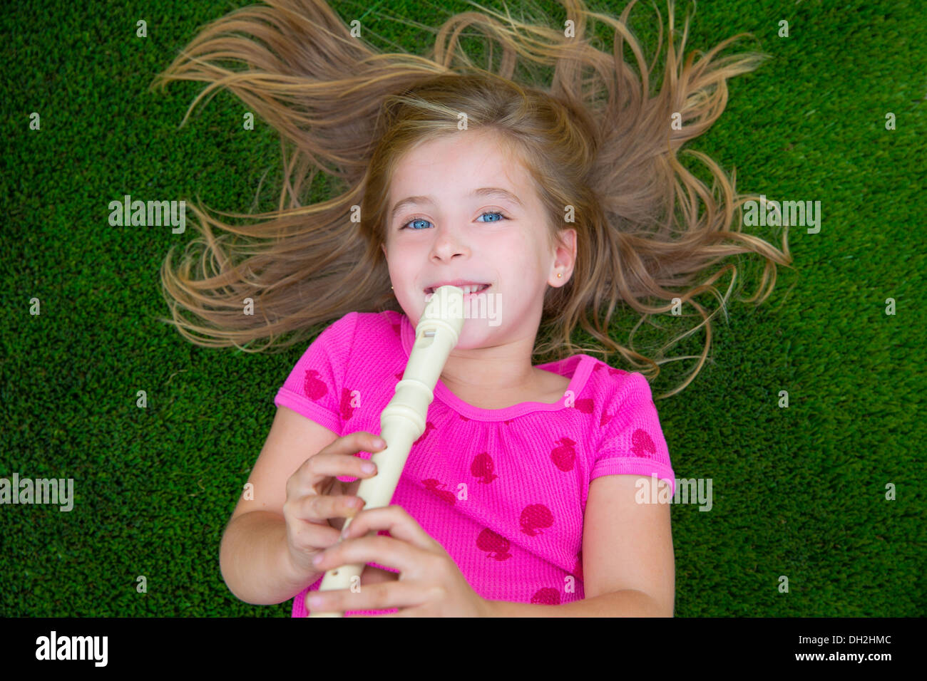 Blond kid children girl playing flute lying on grass backyard lawn ...