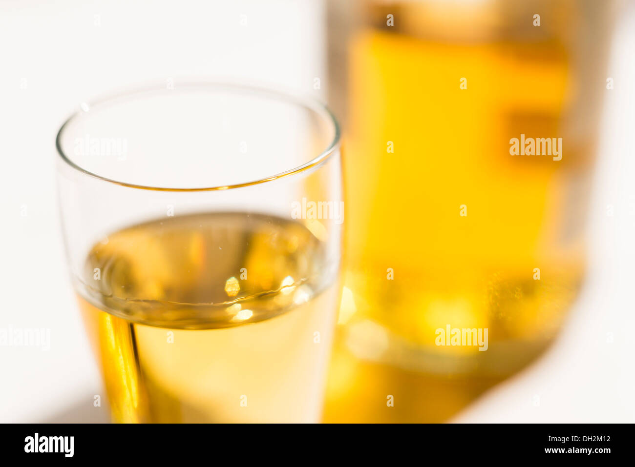 Close-up view of a small glass of liquor, in front of bottle on a white ...