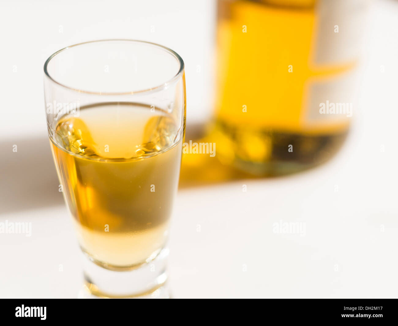 Close-up view of a small glass of liquor, in front of bottle on a white ...