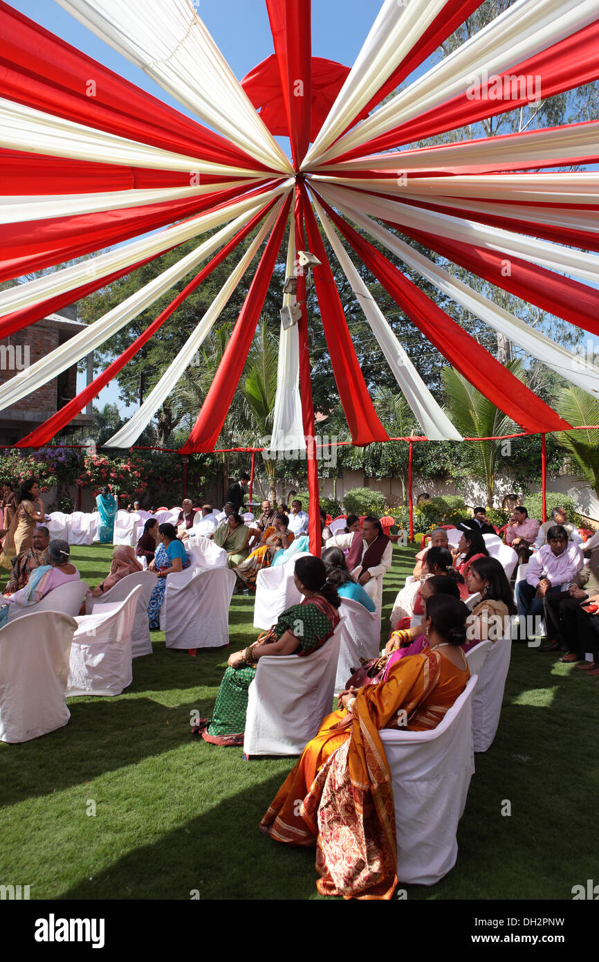 People sitting below red white fabric streamers canopy in Indian ...