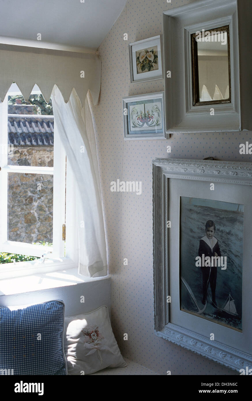 Small mirror and framed photographs on wall beside window with white ...