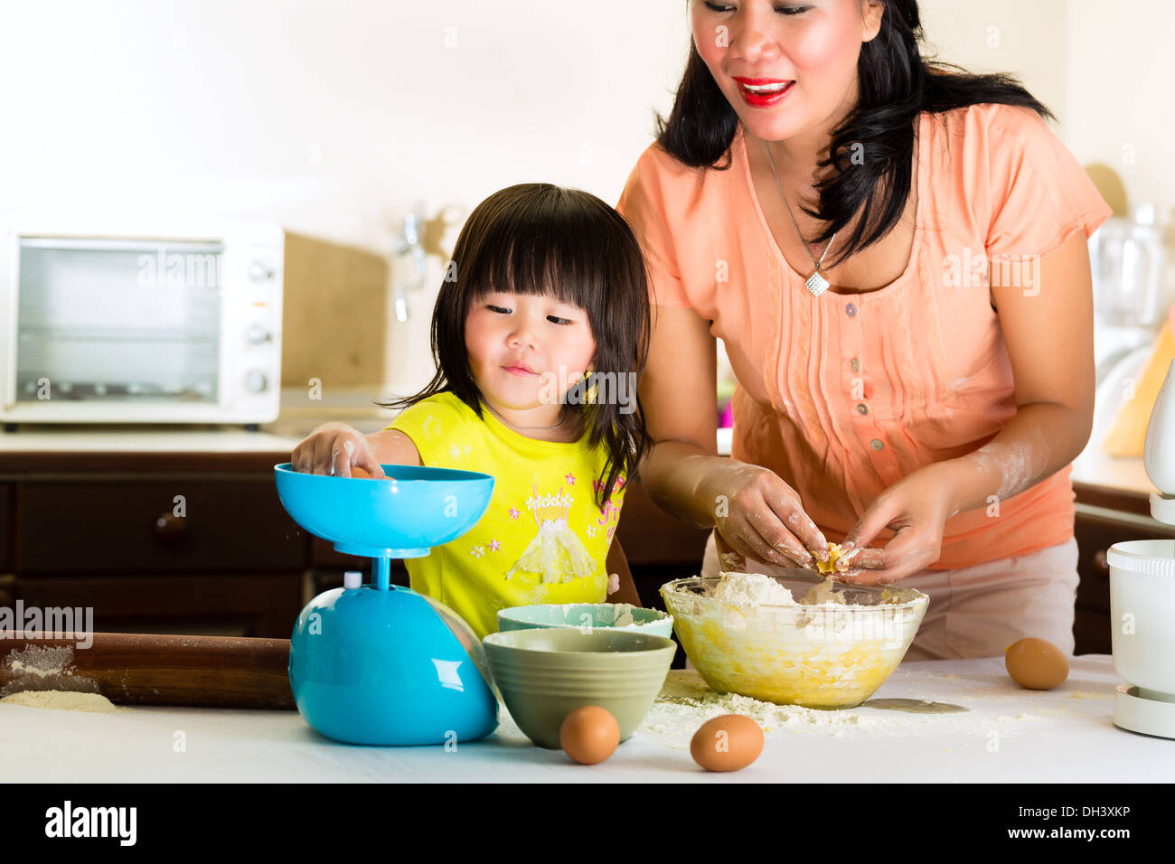 Indonesian Asian Little girl and her mother in the kitchen bake a cake ...