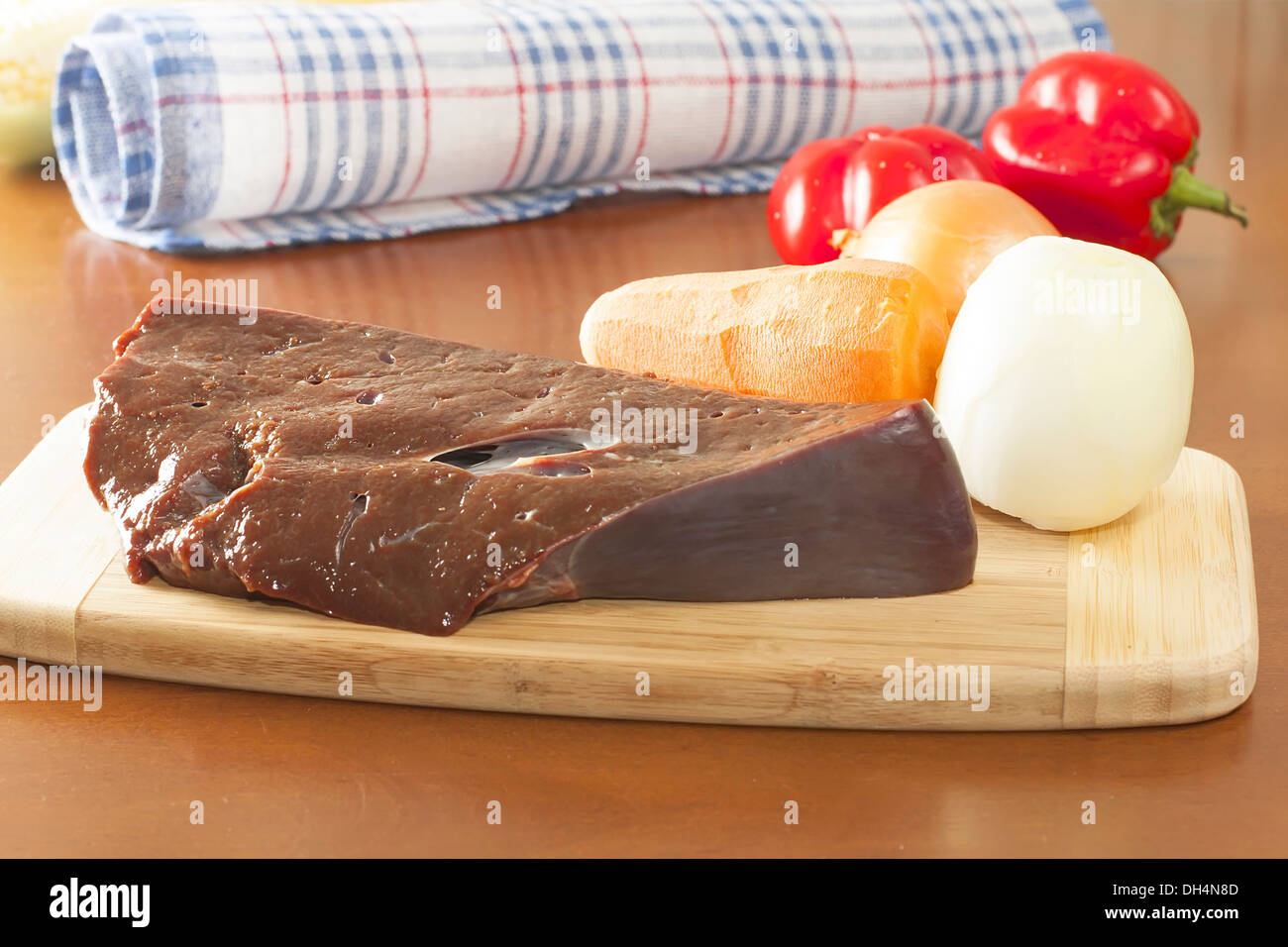 a piece of raw beef liver with vegetables on the cutting board Stock ...
