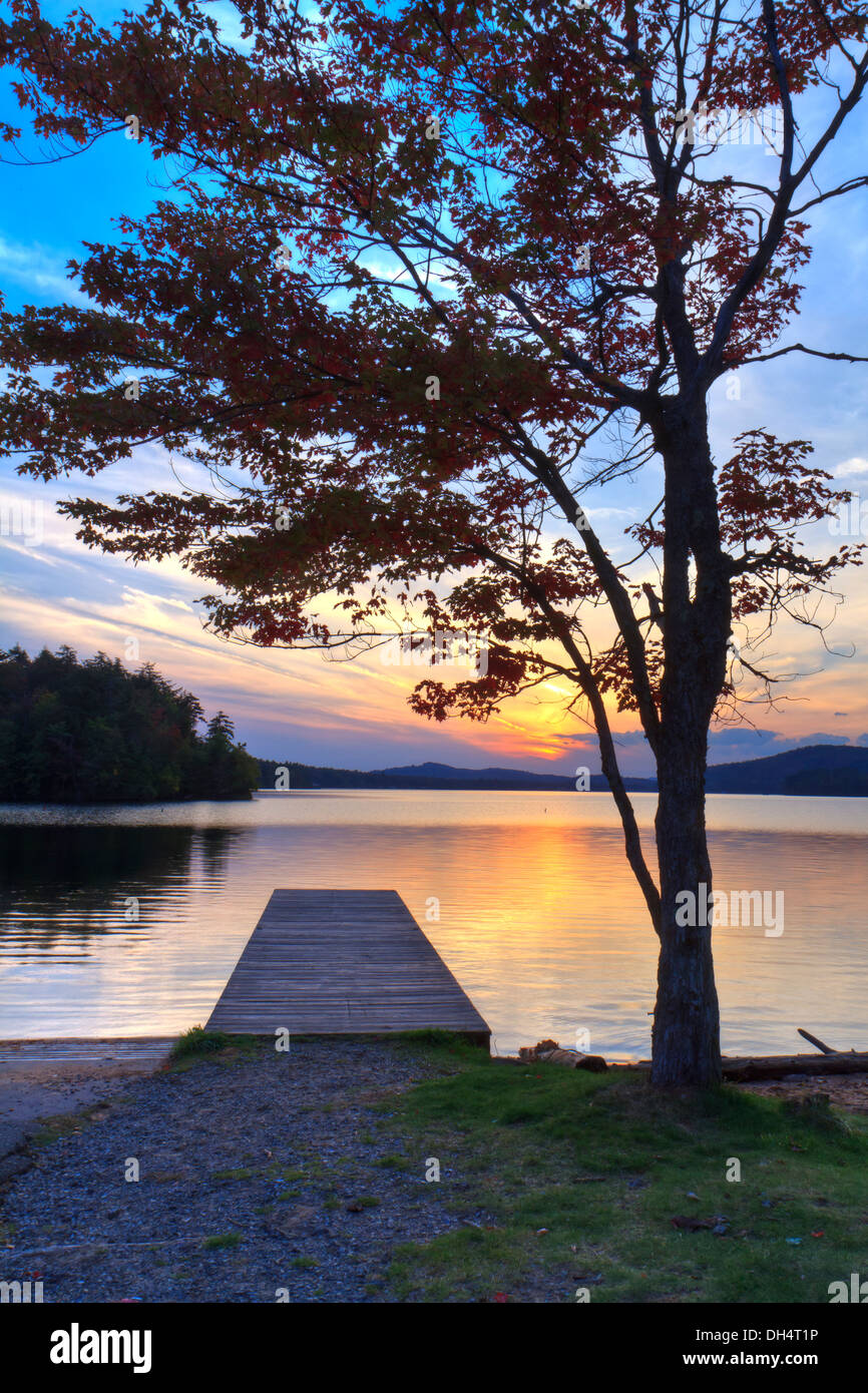 Sun sets behind a dock and maple tree on serene Seventh Lake in the ...