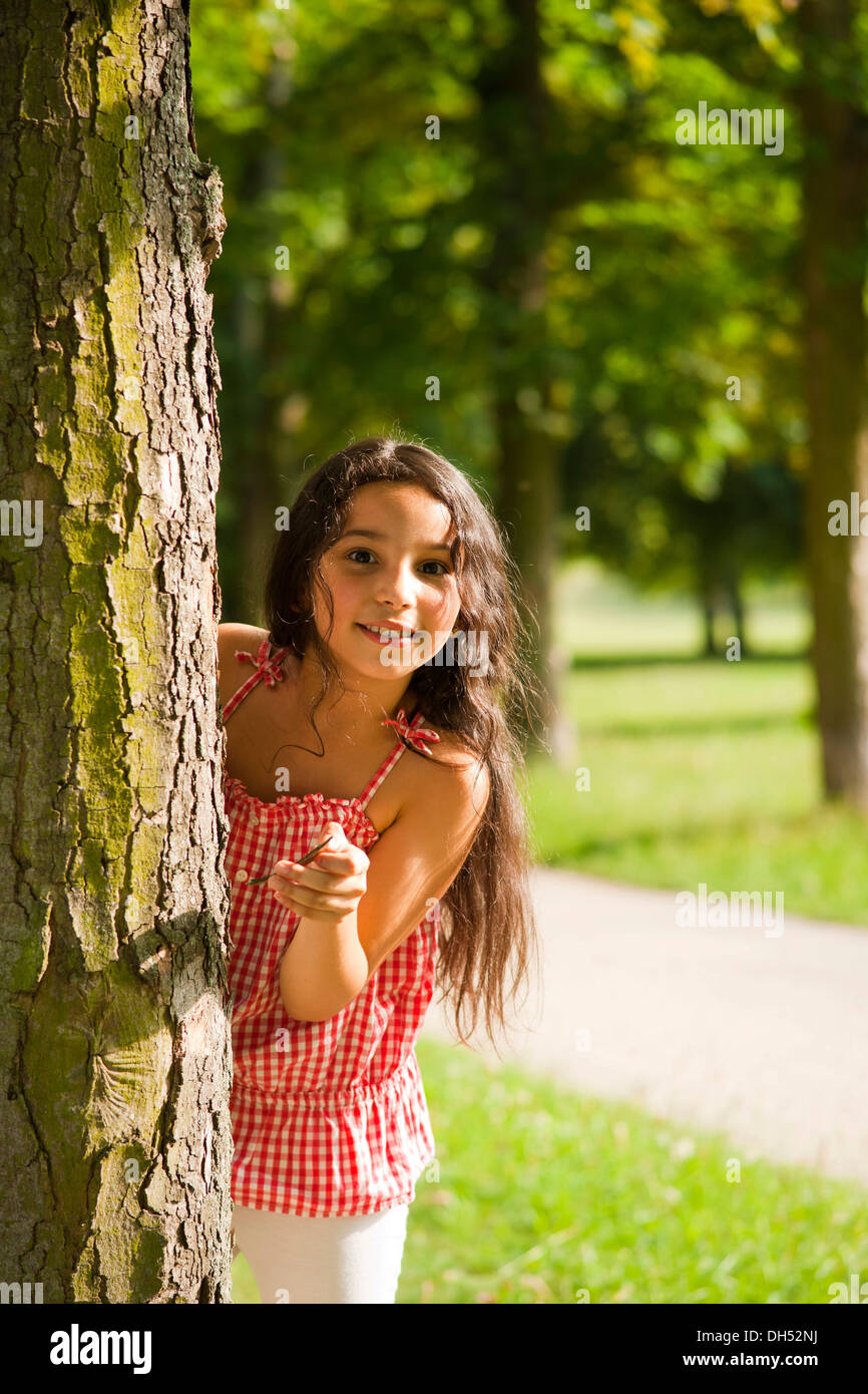Smiling girl looking out from behind a tree Stock Photo - Alamy