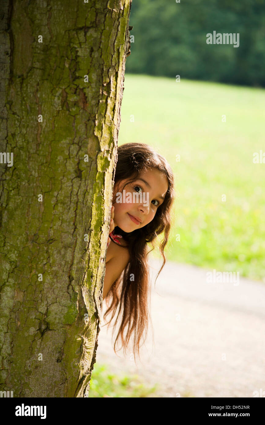 Smiling girl looking out from behind a tree Stock Photo - Alamy