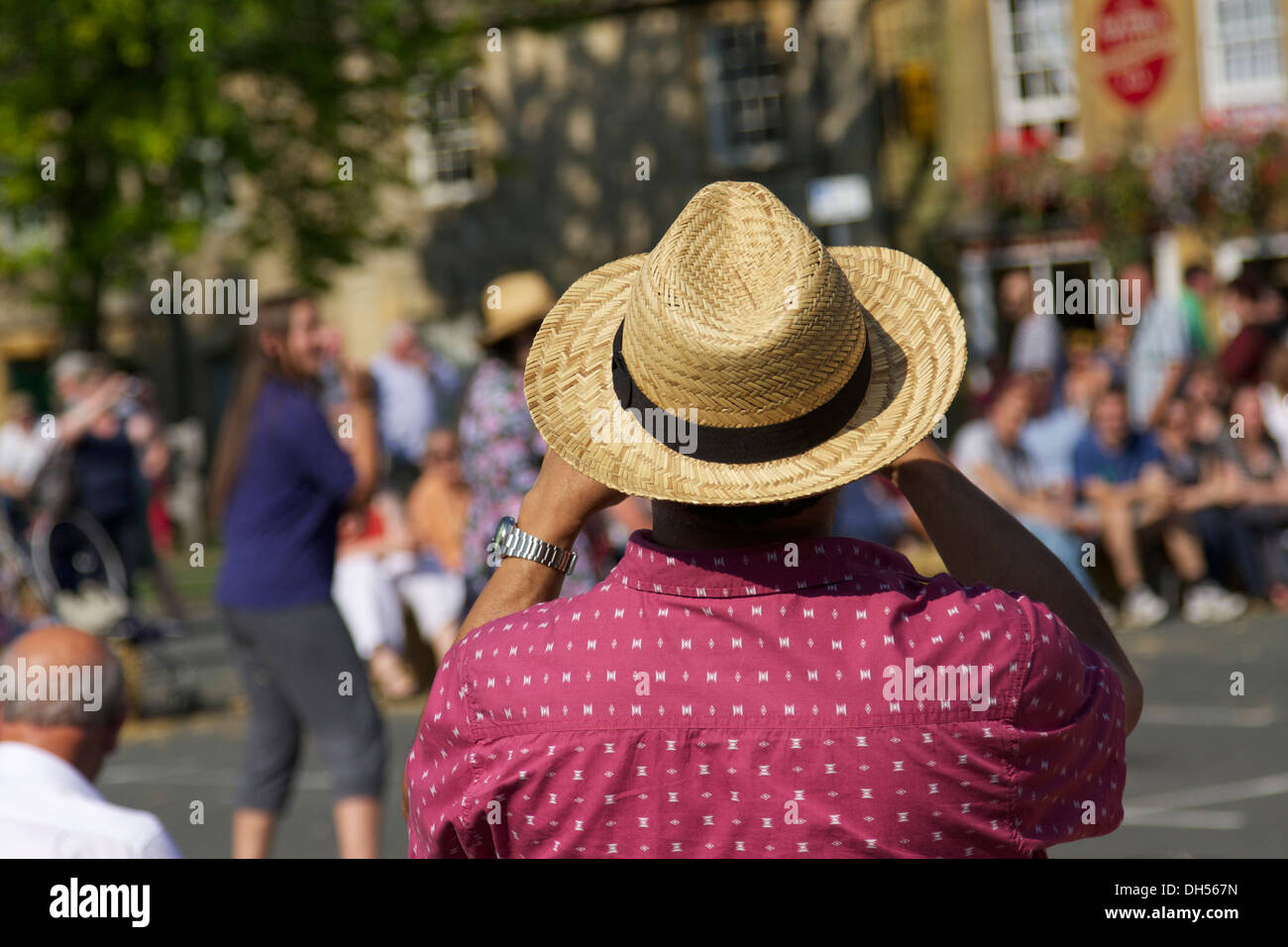 Rear of a man wearing a straw hat and taking a photograph towards a ...