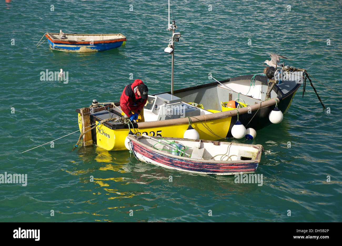 A sailor adjusts his rowing boat from his main boat in St. Ives harbour ...