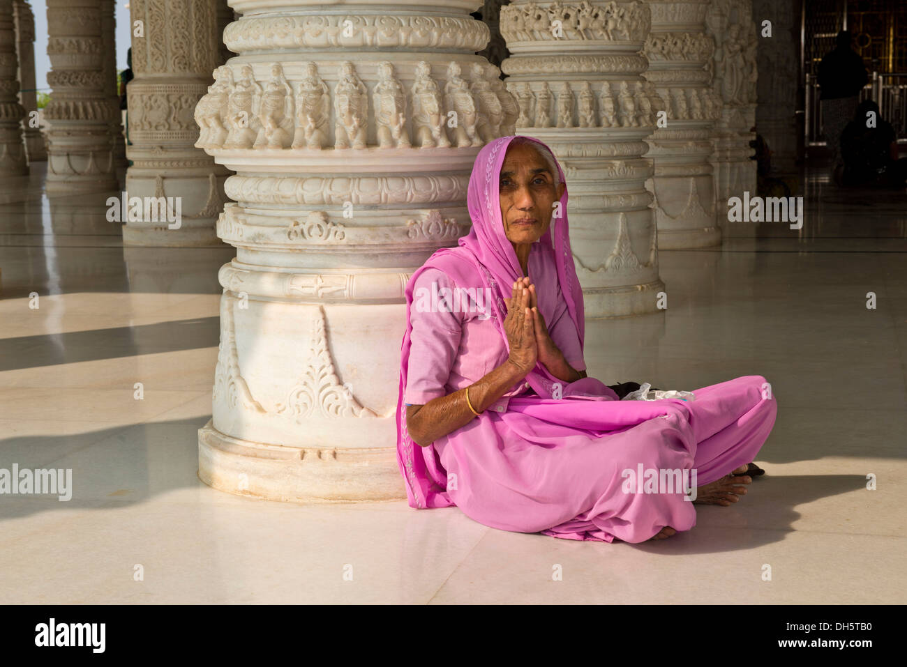 Old Indian woman in a sari sitting on the floor in prayer, in front of ...