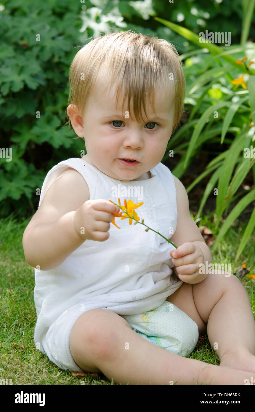 Nine month old baby girl holding and sniffing a crocosmia or montbretia ...