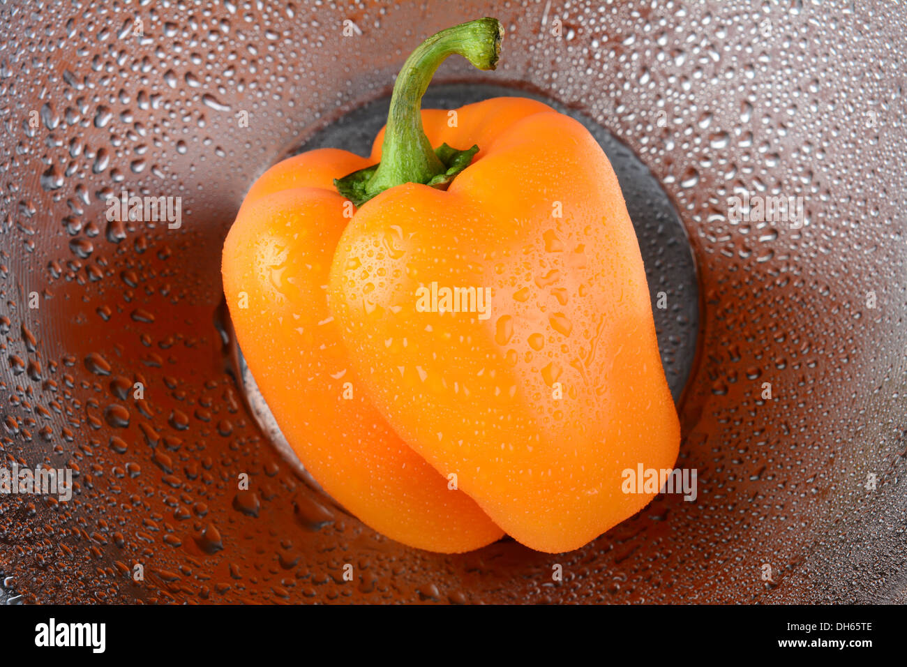 An orange bell pepper in a stainless steel bowl with water drops ...
