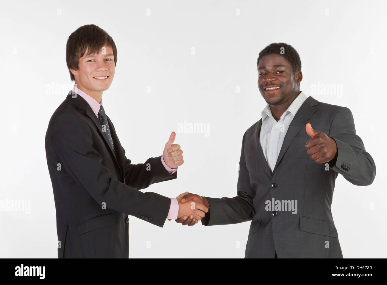 Two young men of different races shaking hands and making a thumbs-up ...