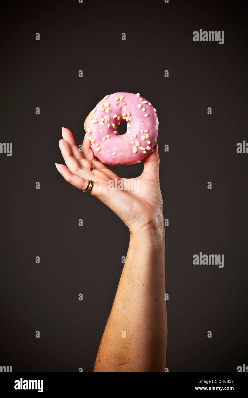 Pink frosted donut being held on a dark grey background Stock Photo - Alamy