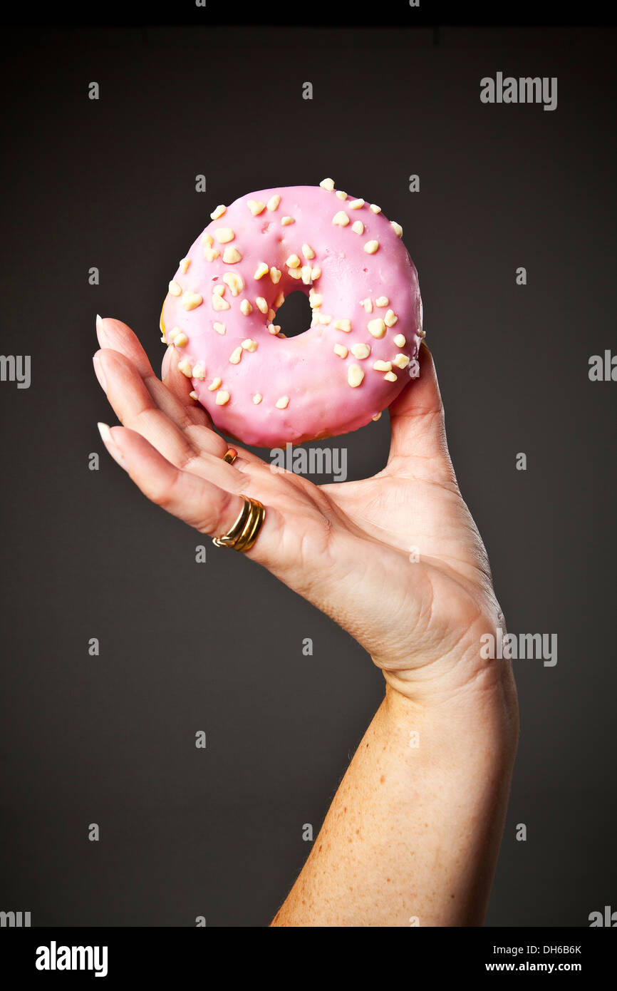Pink frosted donut being held on a dark grey background Stock Photo - Alamy