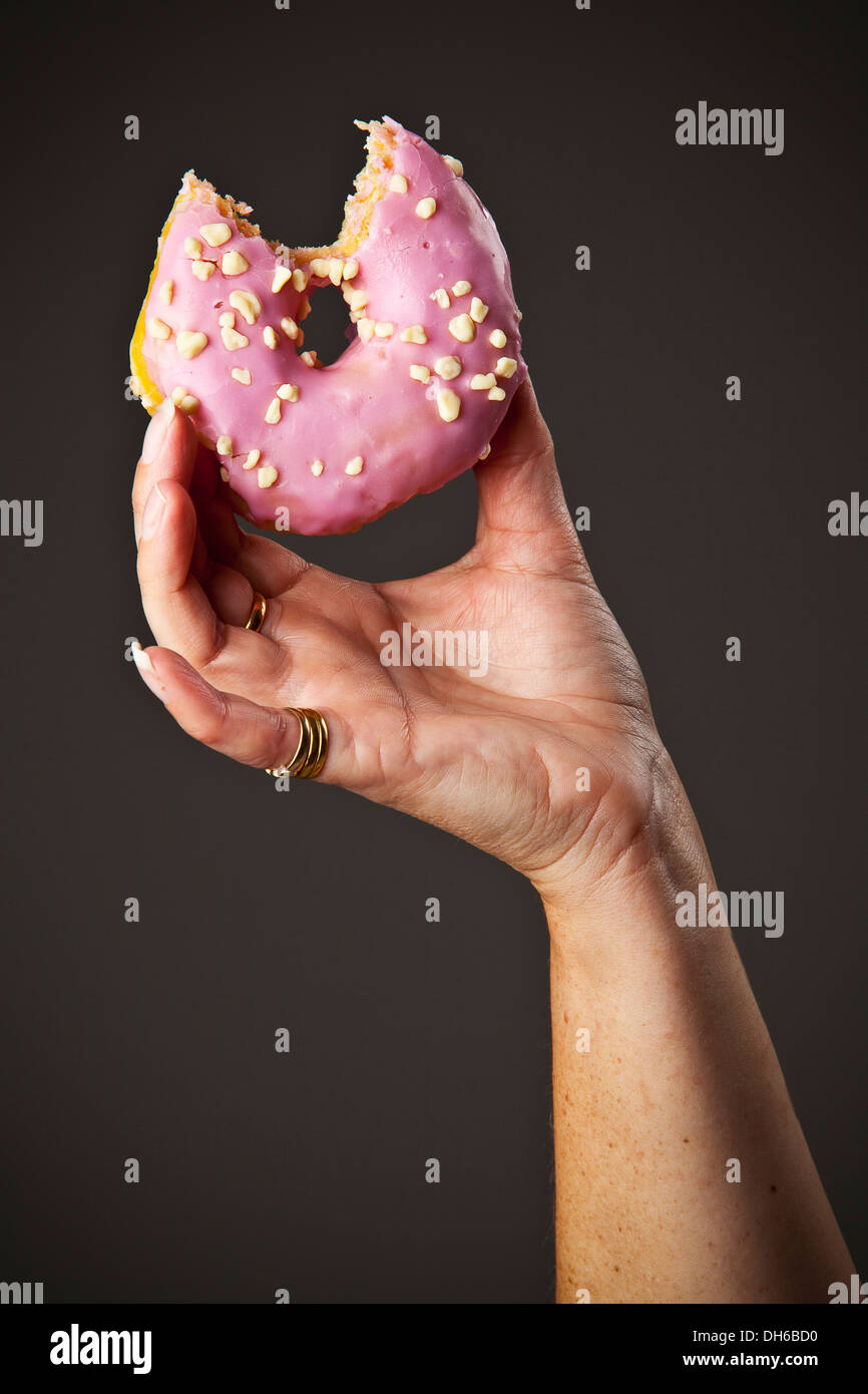 Pink frosted donut being held on a dark grey background Stock Photo - Alamy