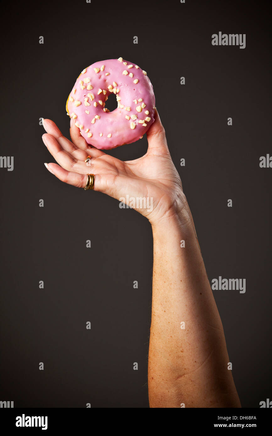 Pink frosted donut being held on a dark grey background Stock Photo - Alamy