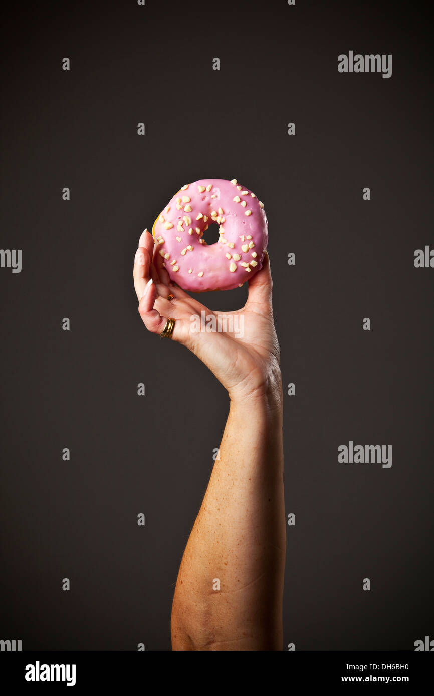 Pink frosted donut being held on a dark grey background Stock Photo - Alamy