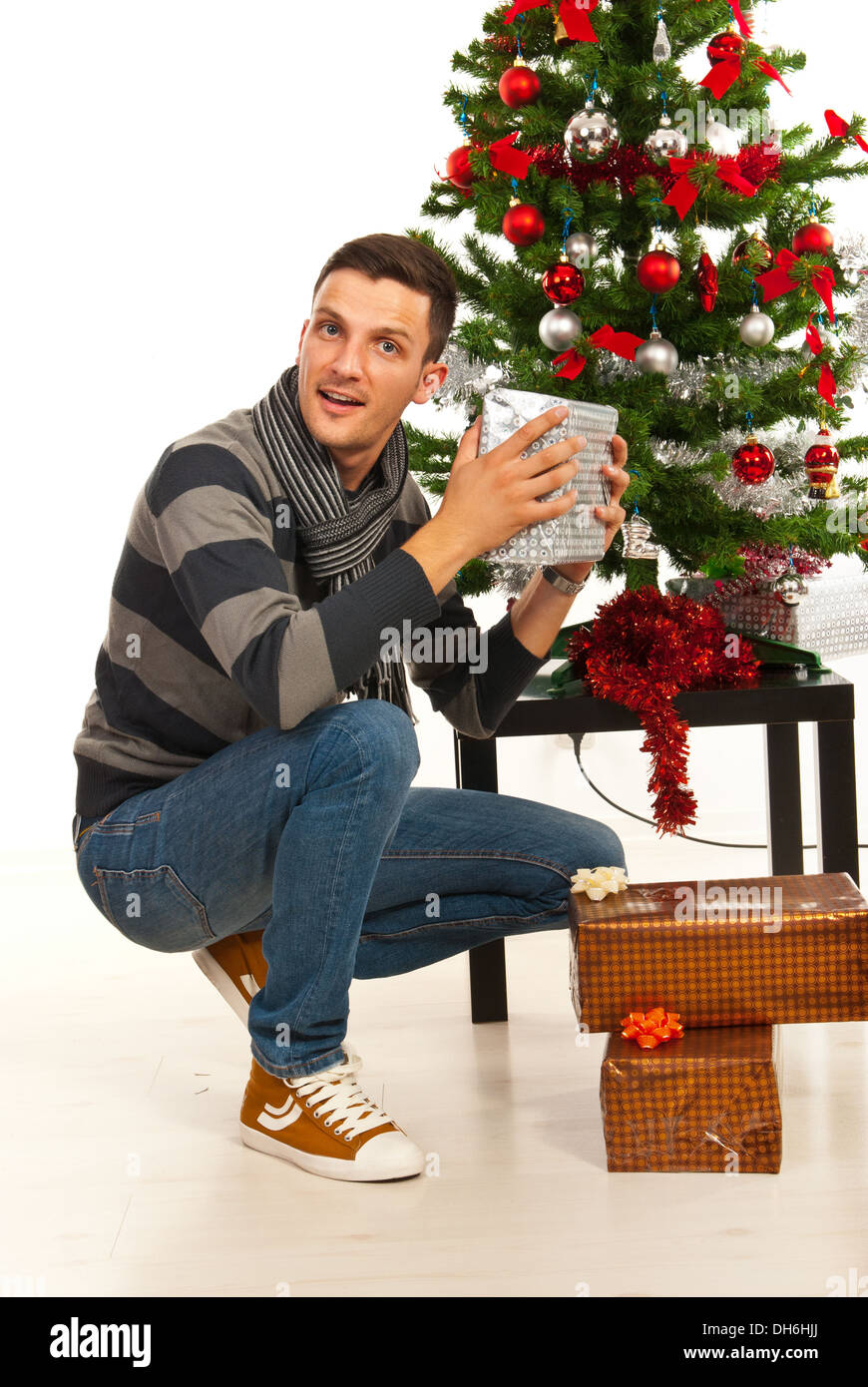 Amazed Christmas man holding gift in front of tree Stock Photo - Alamy