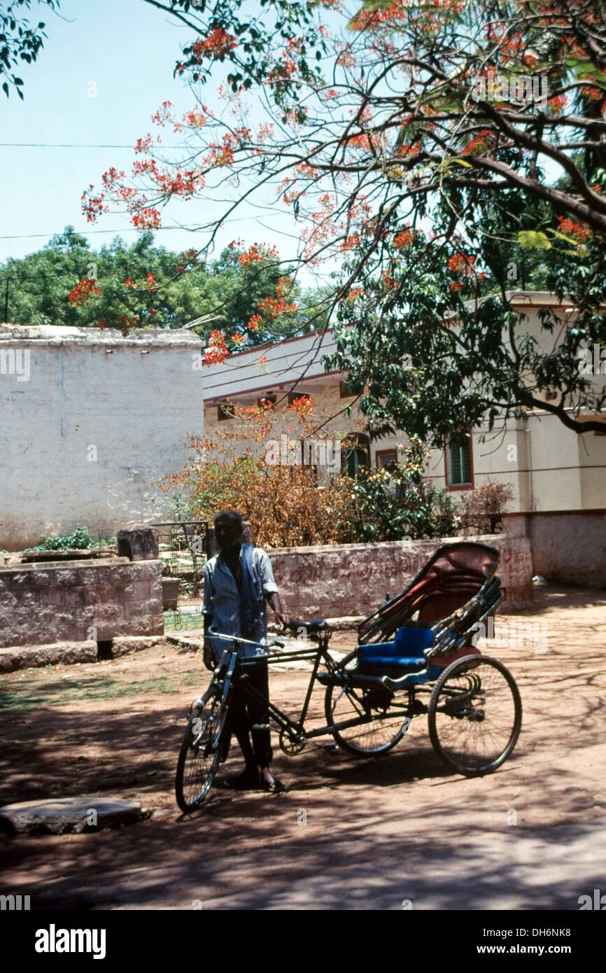 rickshaw owner waiting for a passenger stands under the shade of a ...